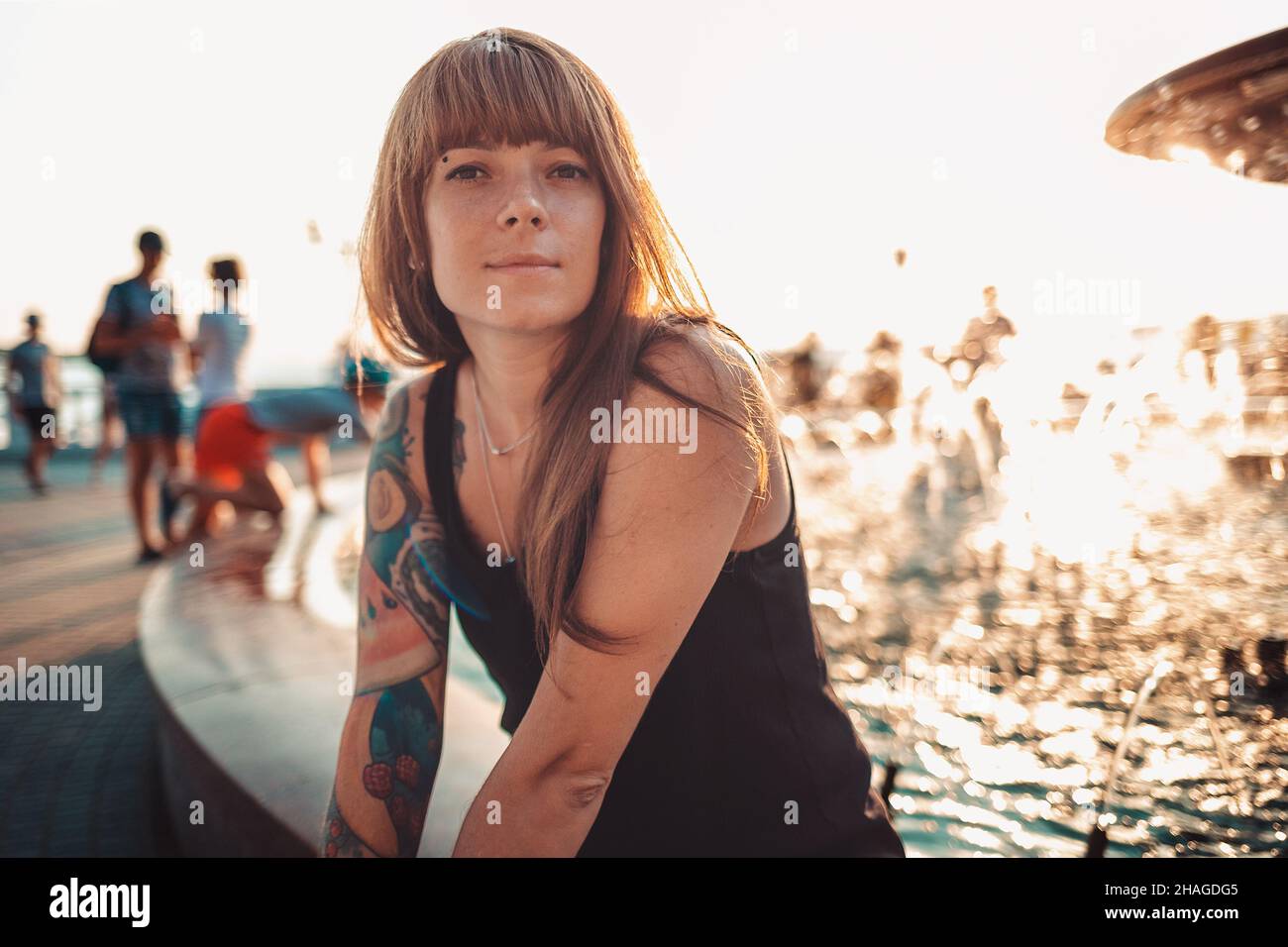 Portrait of tanned young woman with a tattoo on her arm is sitting by ...