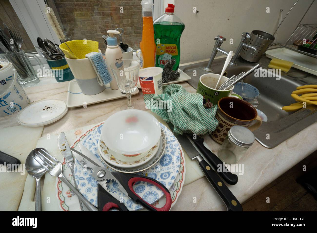kitchen worktop and sink with washing up of dirty plates cups knives ...