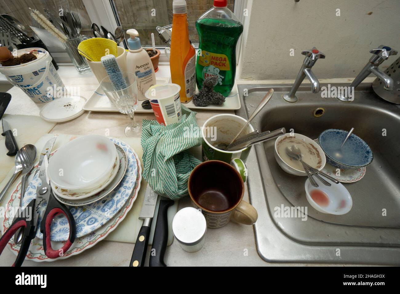 kitchen worktop and sink with washing up of dirty plates cups knives ...