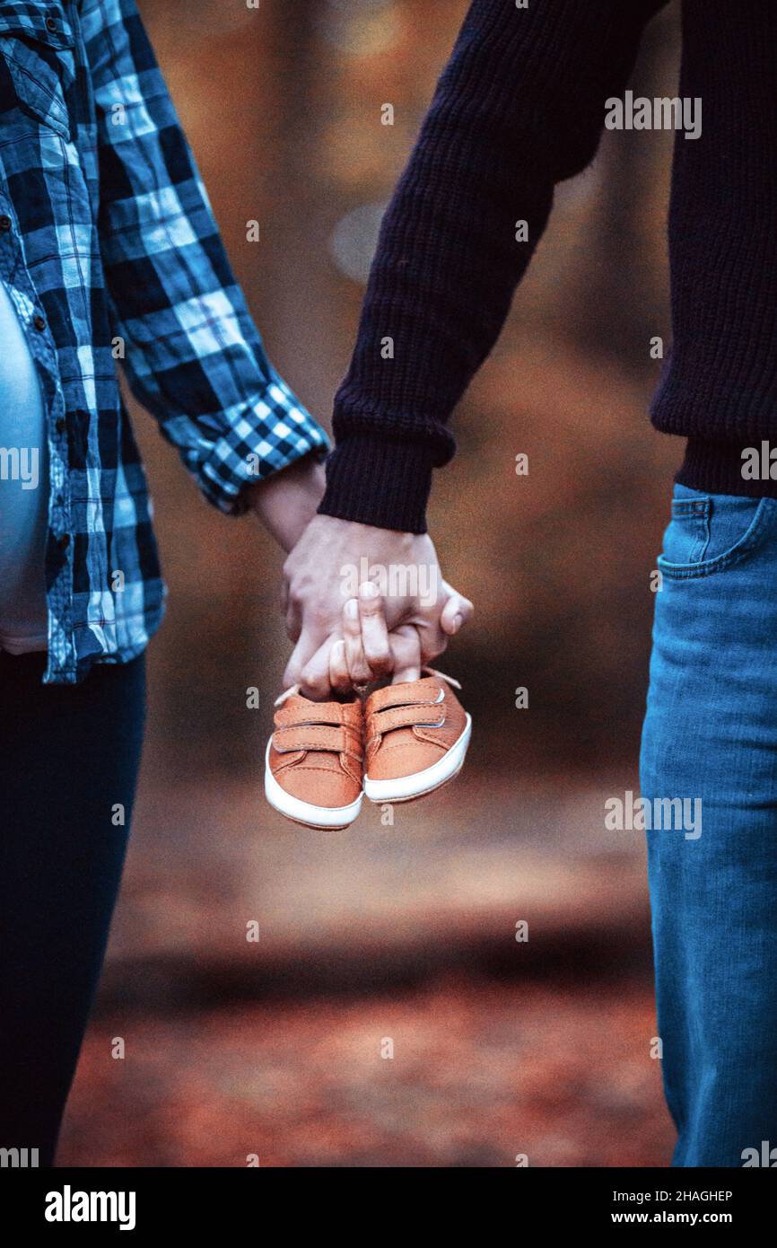 Vertical shot of a couple holding baby shoes indicating the birth of a ...