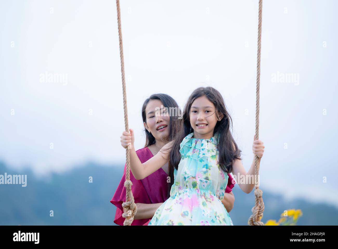 Happy girl playful swinging on a swing. Mother and daughter enjoying summer day at a playground ...