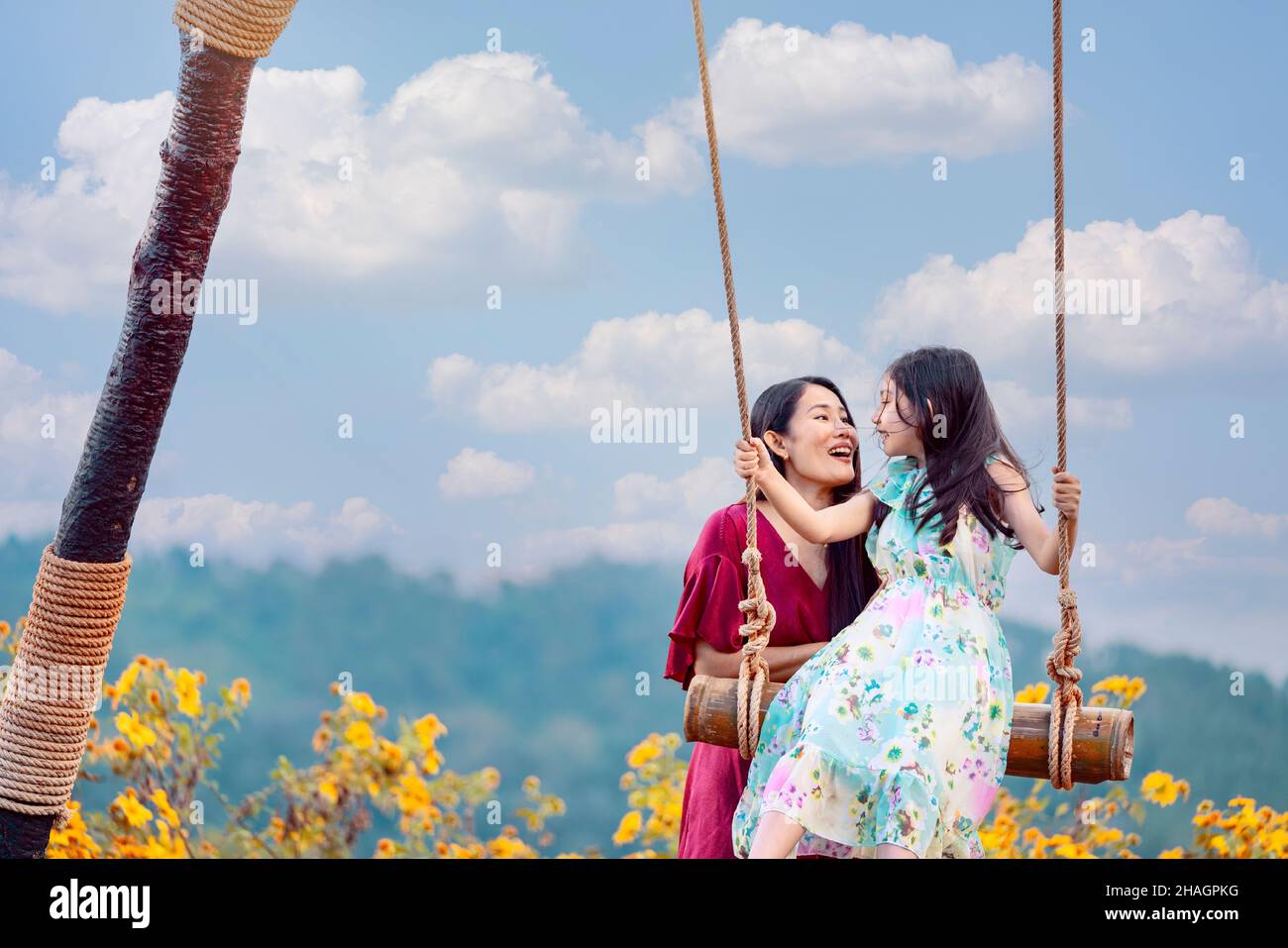 Happy girl playful swinging on a swing. Mother and daughter enjoying summer day at a playground ...