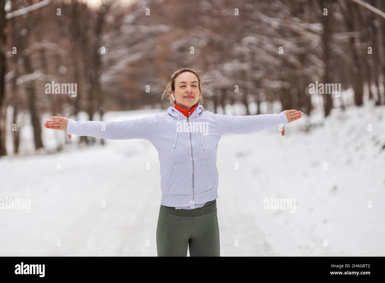Fit sportswoman standing in nature on snow at winter day and doing warm ...