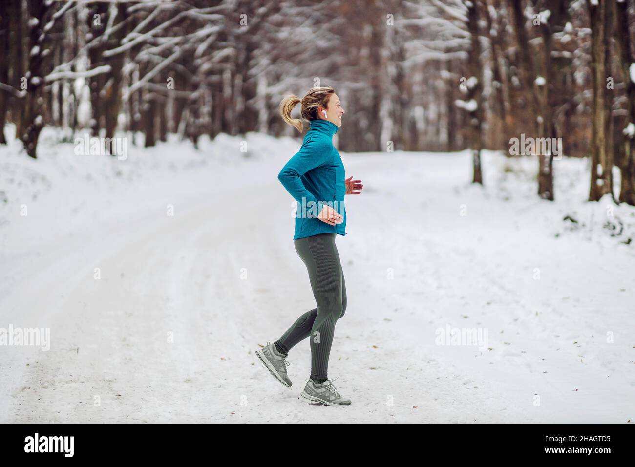 Side view of sportswoman jogging in woods on a snowy chilly winter day ...