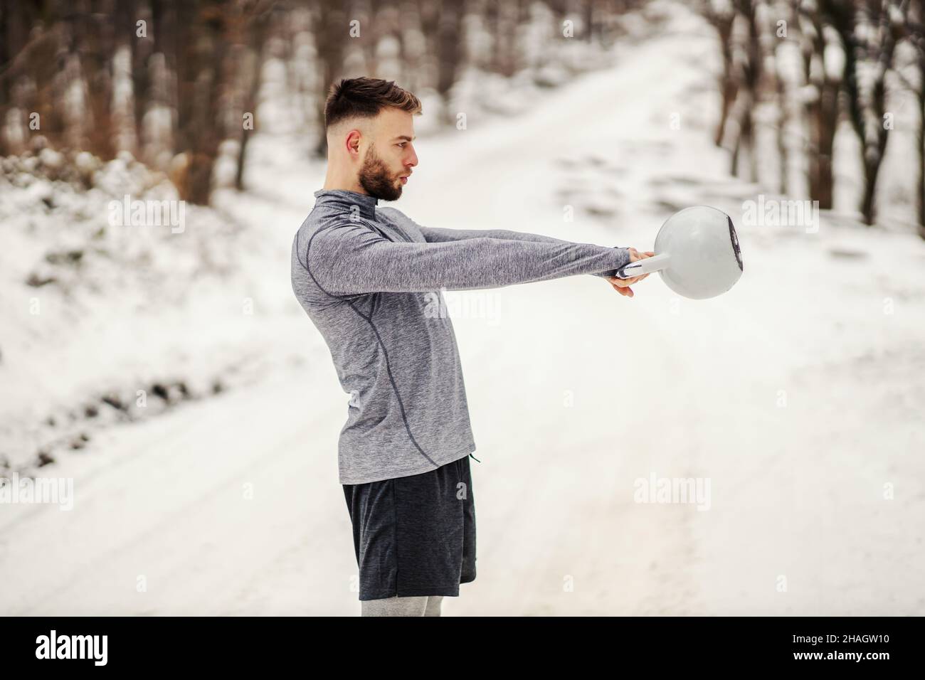 Fit bodybuilder standing on snowy path in forest and swinging ...