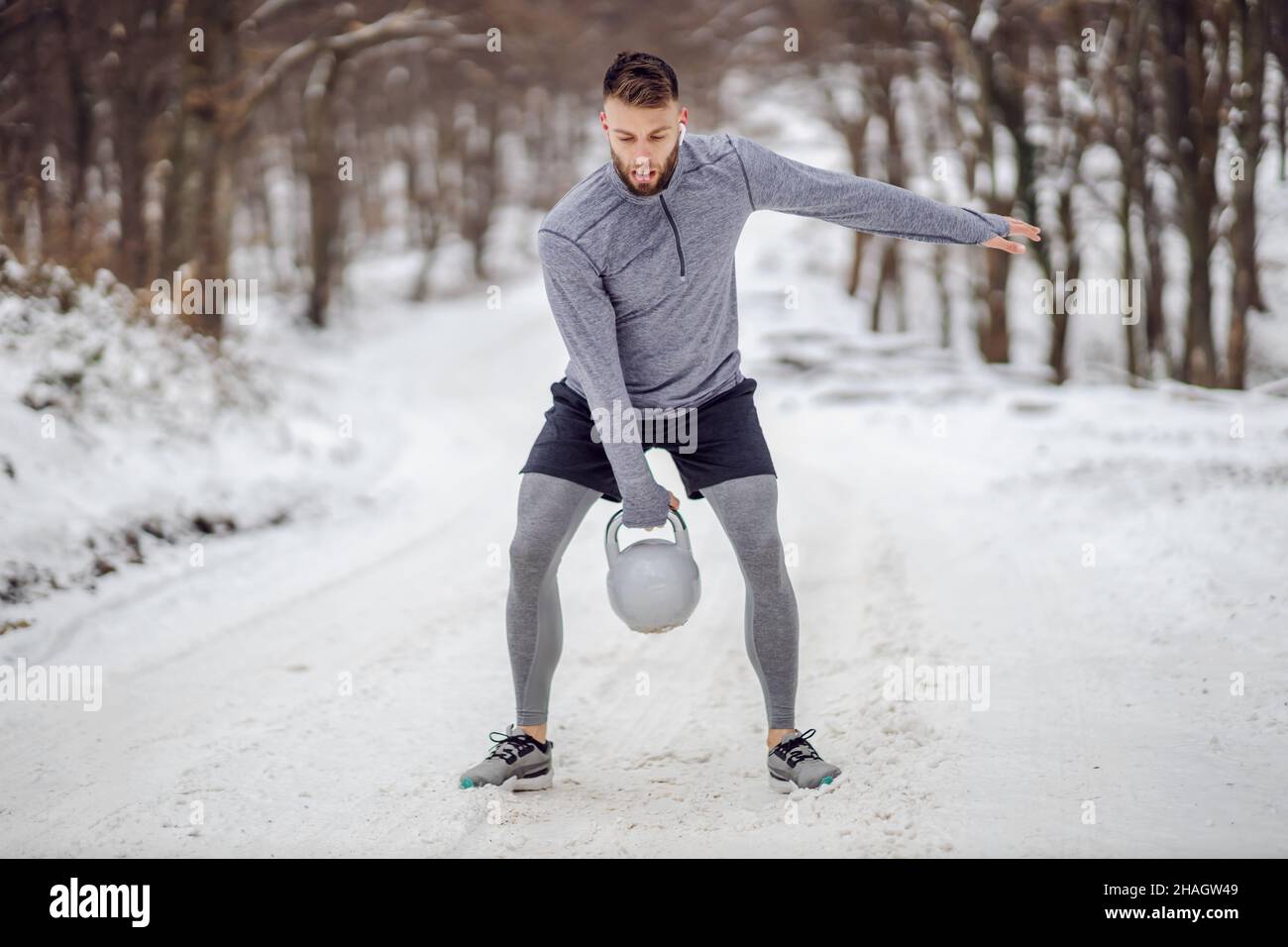 Fit bodybuilder standing on snowy path in forest and swinging ...