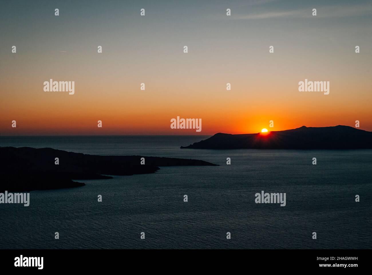 The sun sets behind an island in the sea, Santorini, Greece Stock Photo ...