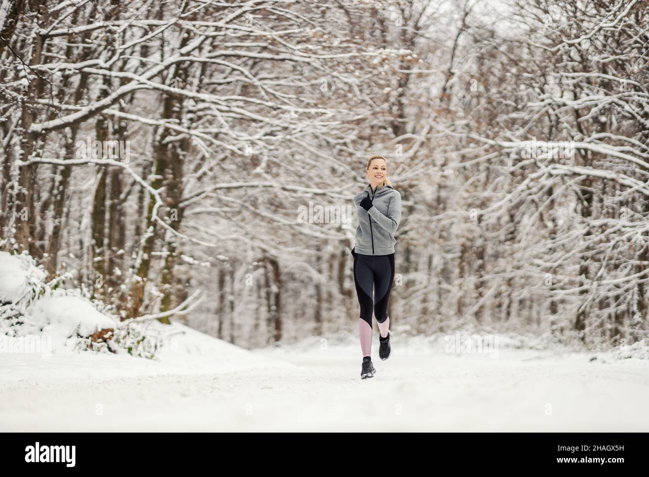 Happy fit sportswoman jogging in nature on snowy path at winter ...