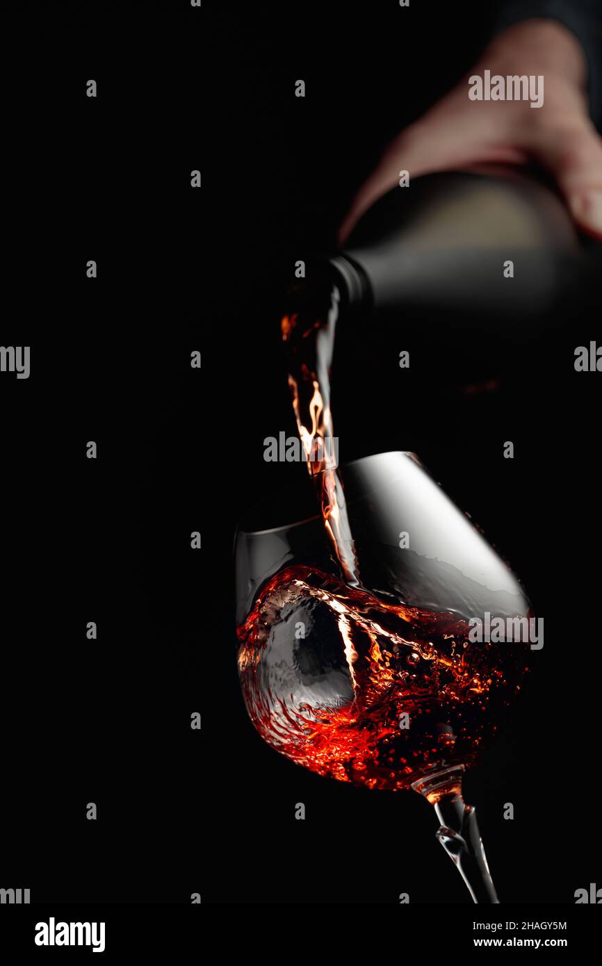 Pouring brandy in a glass goblet. Black background with copy space ...