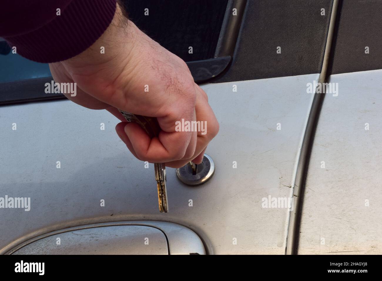 A man's hand inserts a key into the keyhole of a used car door. There ...