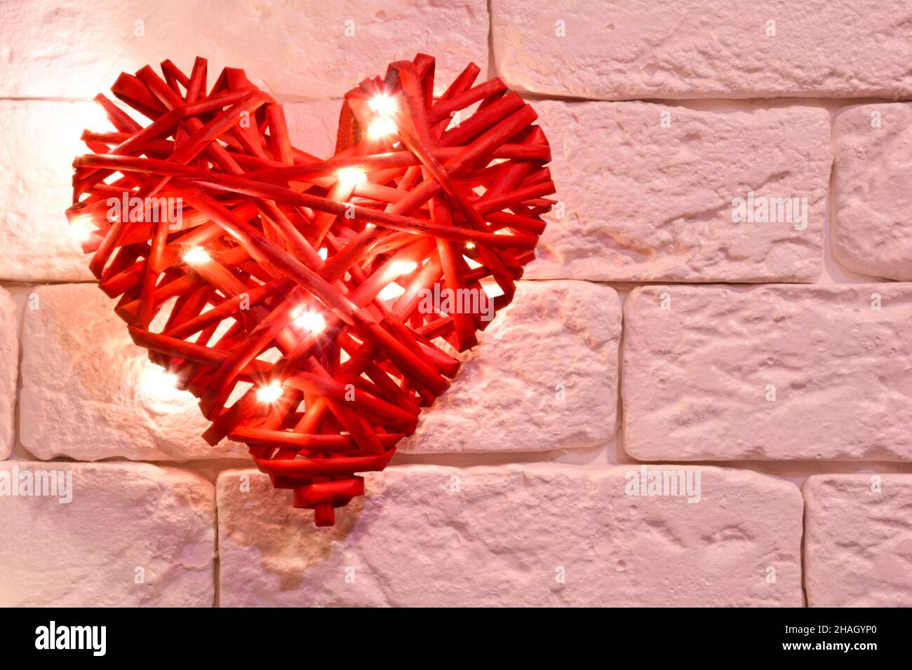 Handmade red wicker decorative heart, illuminated by lights against a ...