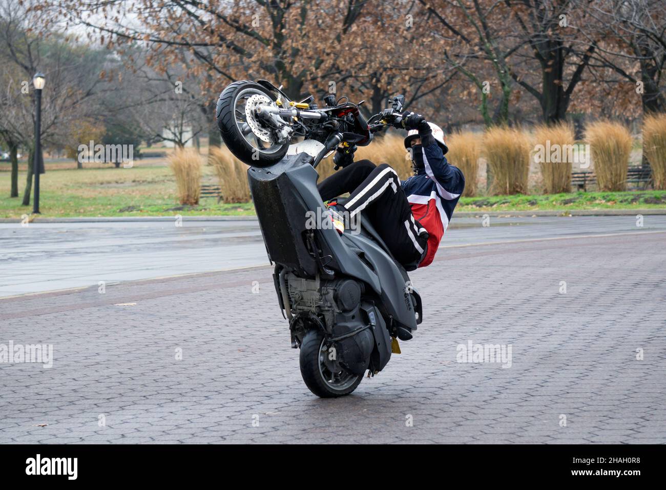 A teenage biker with a helmet & mask does a wheelie on his Yamaha TMax ...