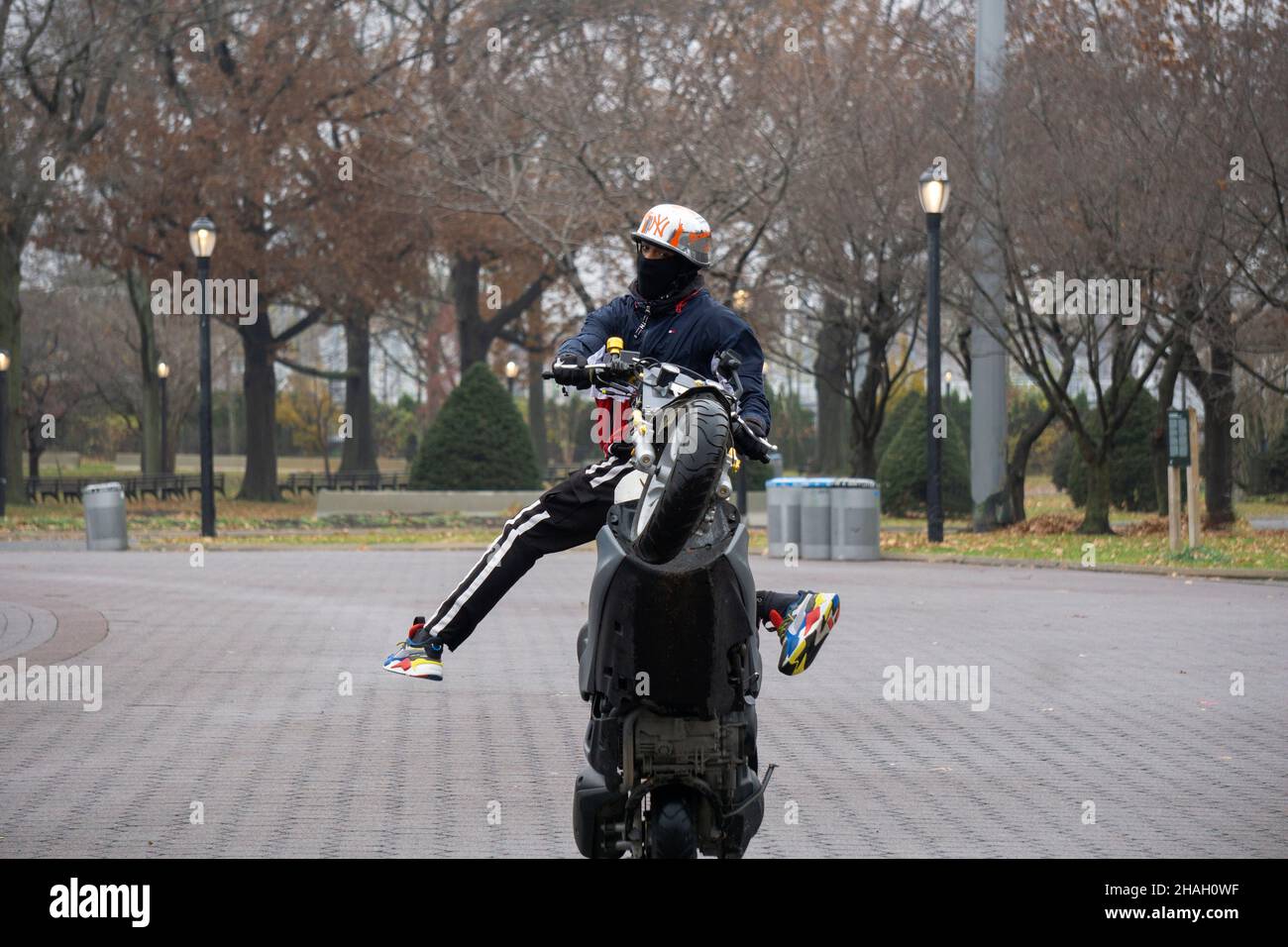A teenage biker with a helmet & mask does a wheelie on his Yamaha TMax ...