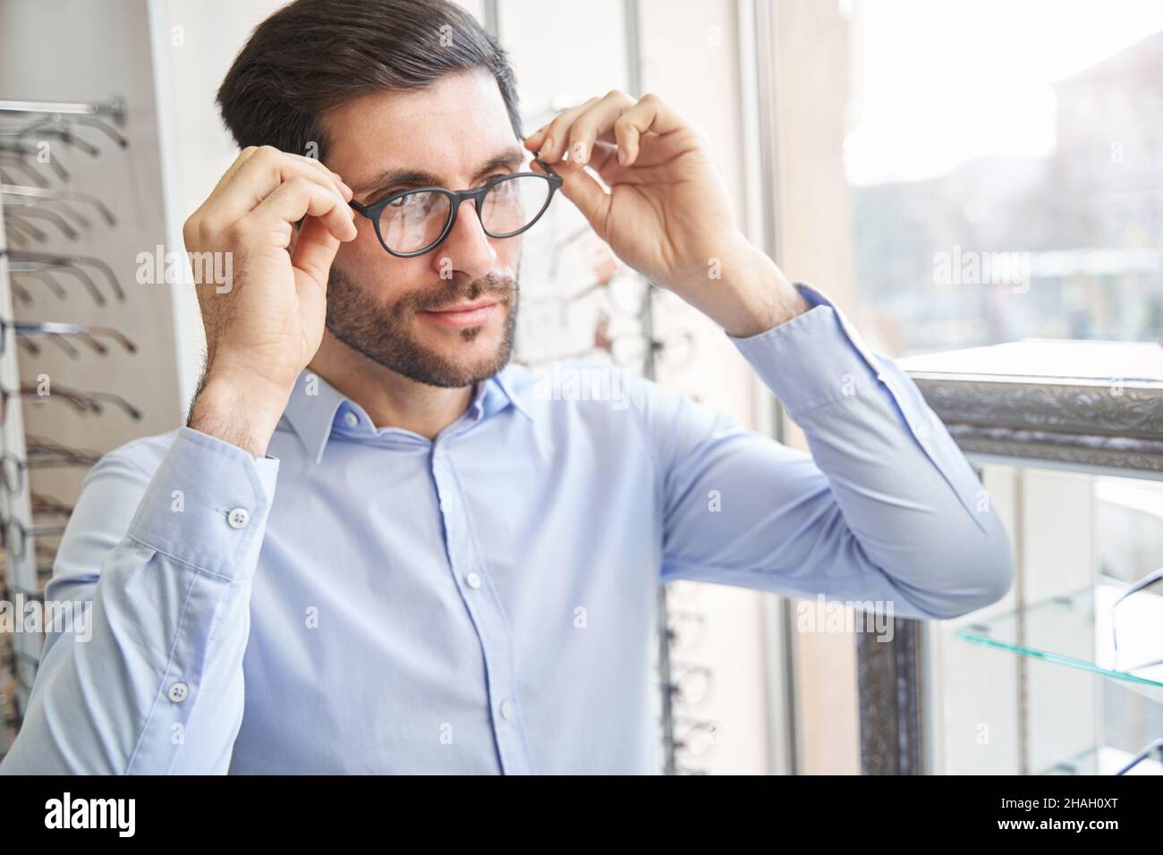Man putting on eyeglasses next to window Stock Photo - Alamy