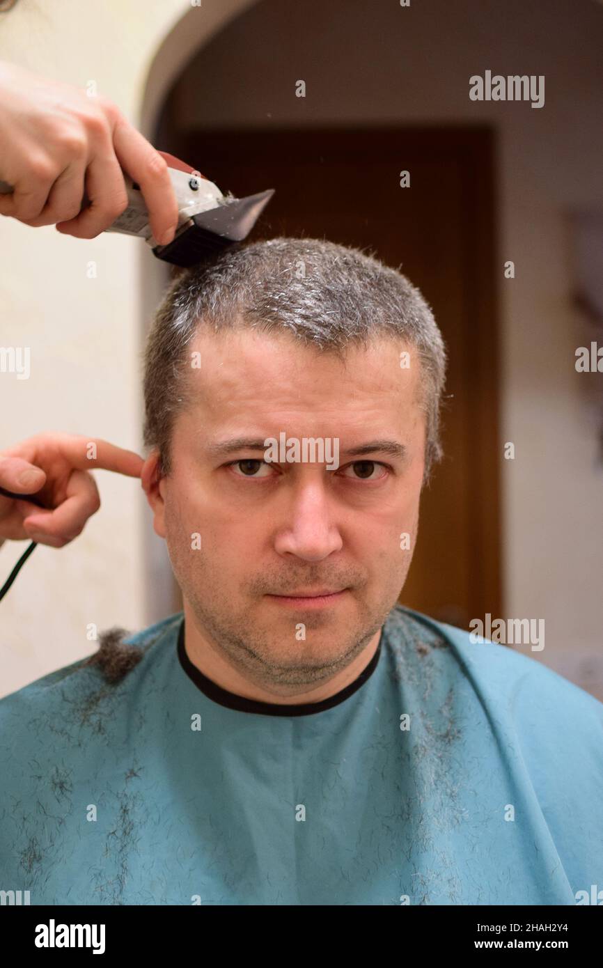 A grown man is trimmed with a hair clipper and sits facing the camera ...