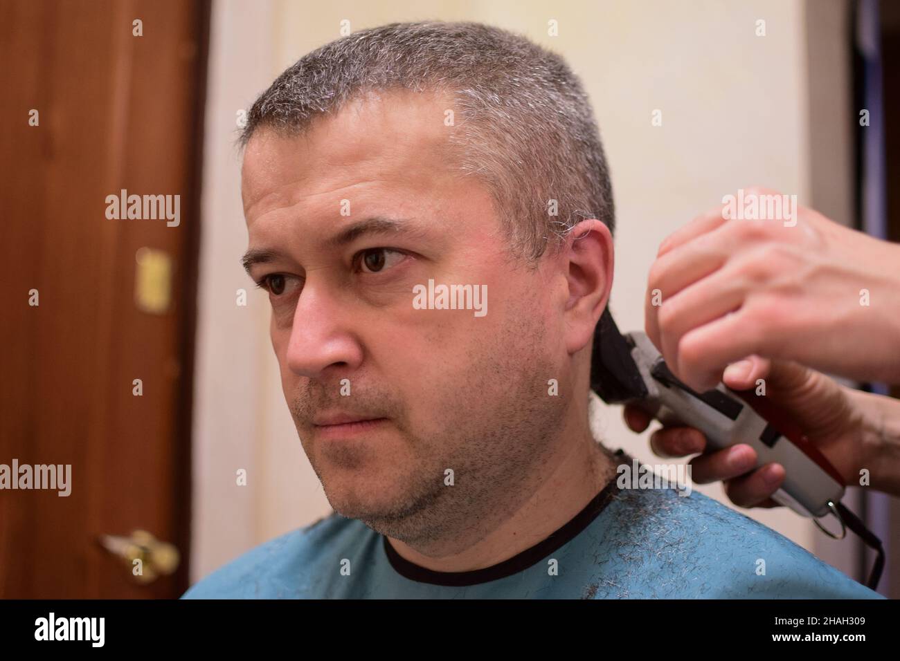 A grown man is trimmed with a hair clipper and sits facing the camera ...