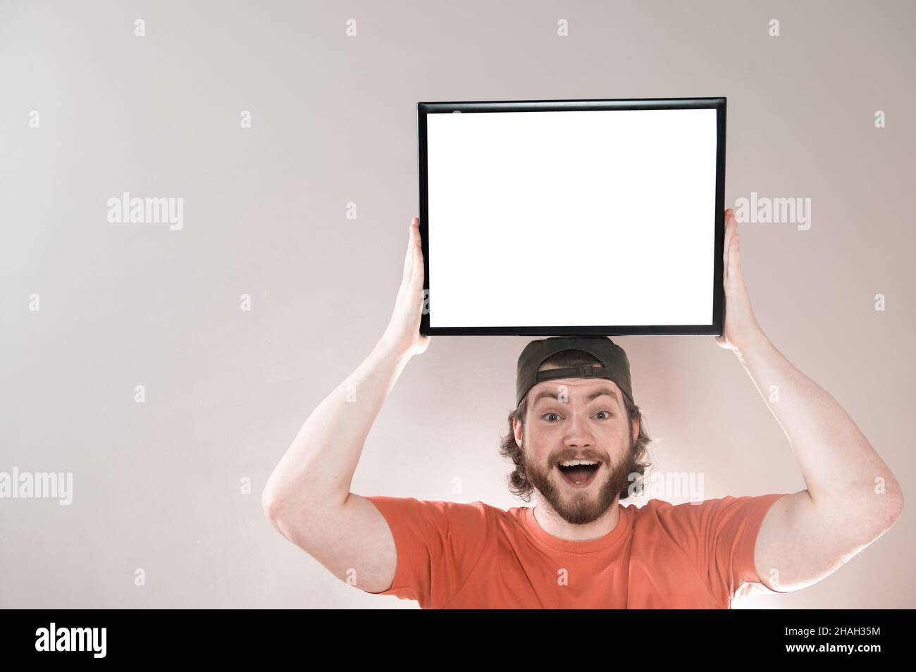 Young bearded man making funny face, holding a blank sign board on head ...
