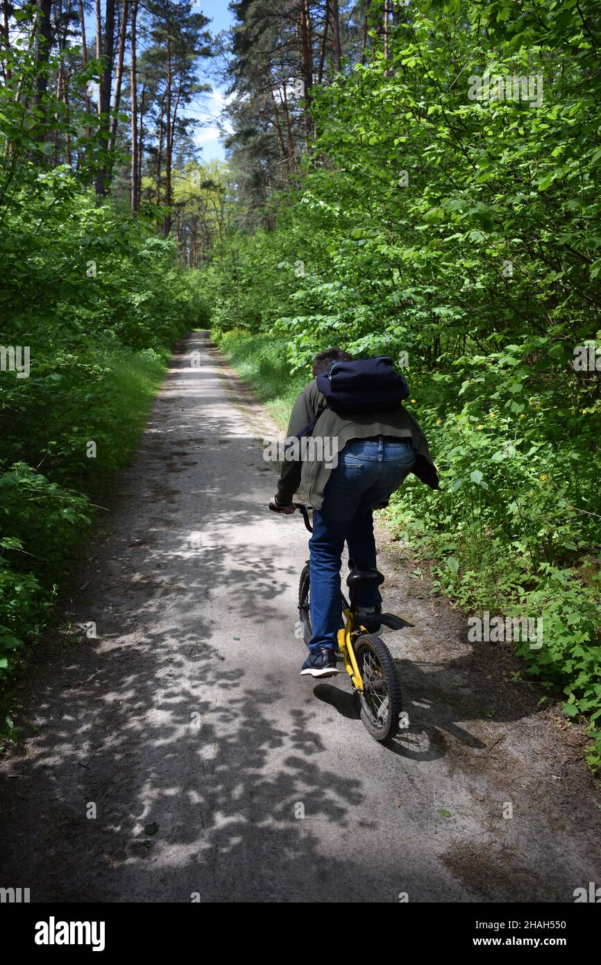 A teenager about 14 years old funny rides a child's bike along a forest ...