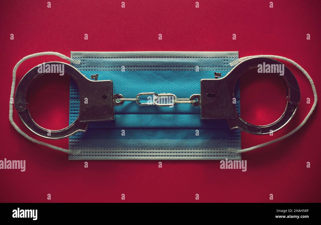Handcuffs laying on a surgical mask in a red background Stock Photo - Alamy