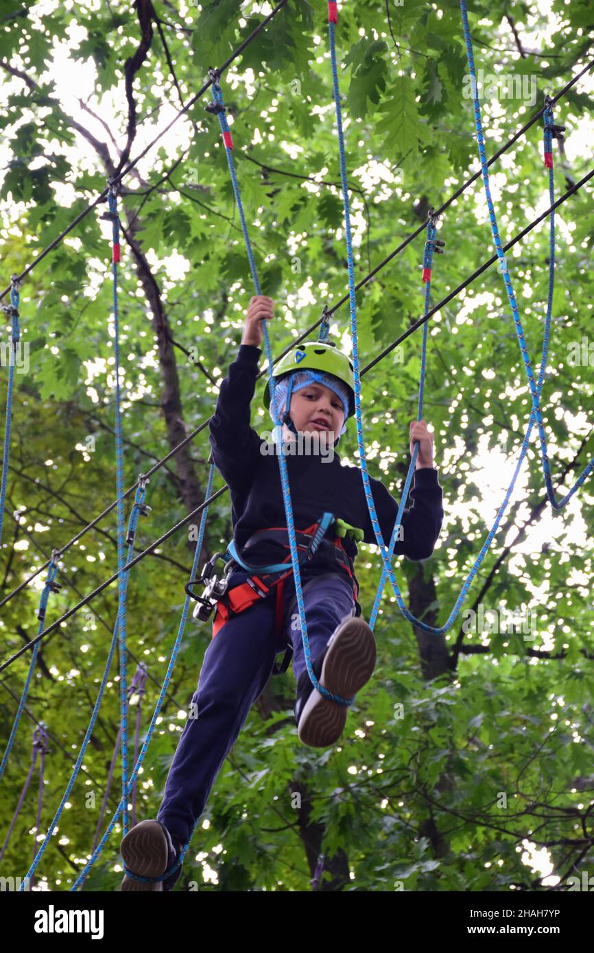 A teenage boy in a safety helmet climbs a hanging ladder in a rope ...