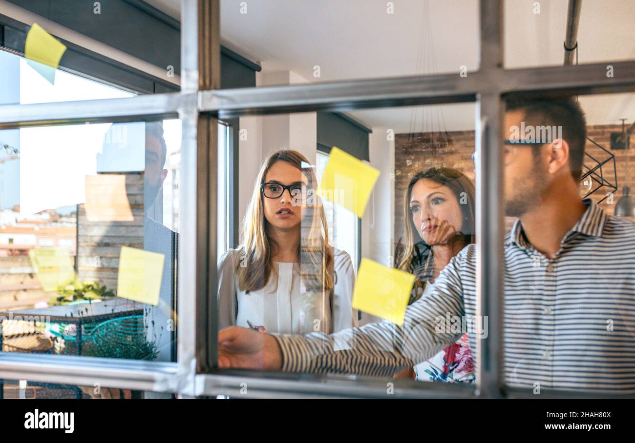 Business people in a work meeting placing sticky notes on the wall ...