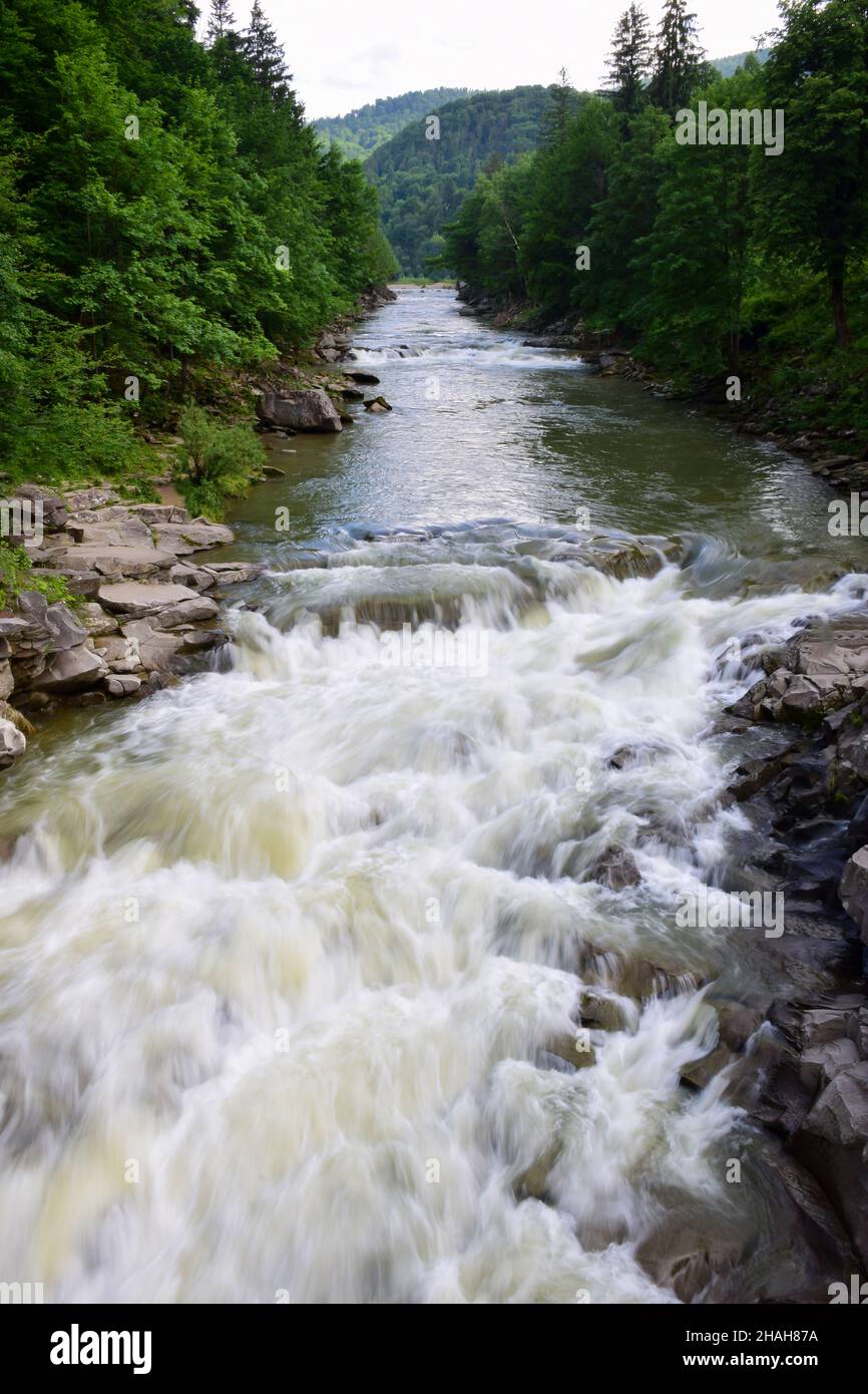 A stormy stream of a mountain river with a foamy waterfall flows ...