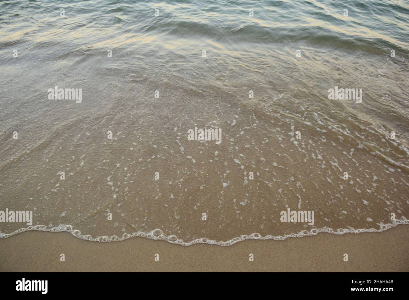 A small sea wave rolls over the sandy beach with transparent water with ...