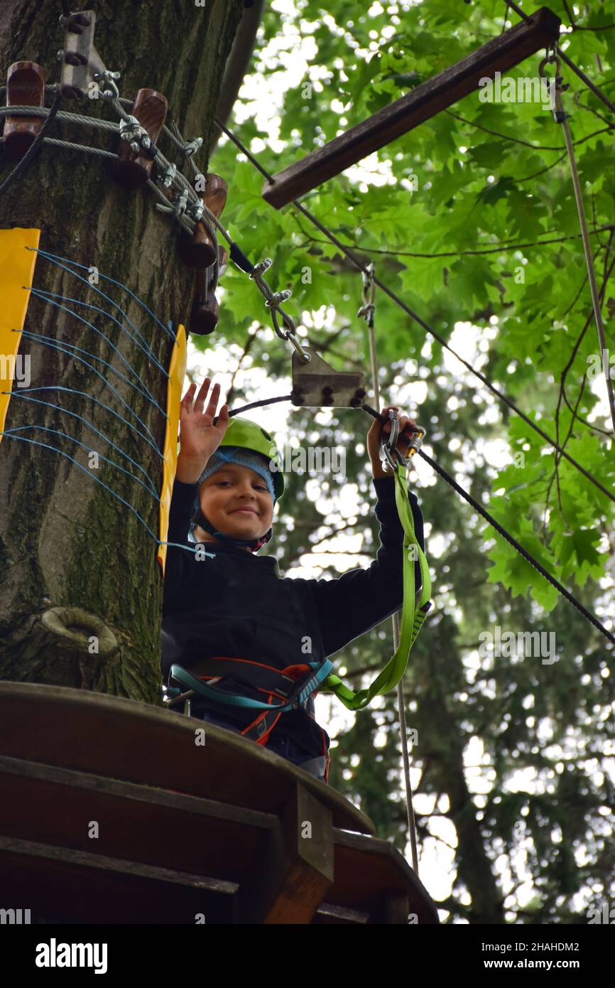 Young teen boy climbs hanging stairs from one tree to another in a rope ...