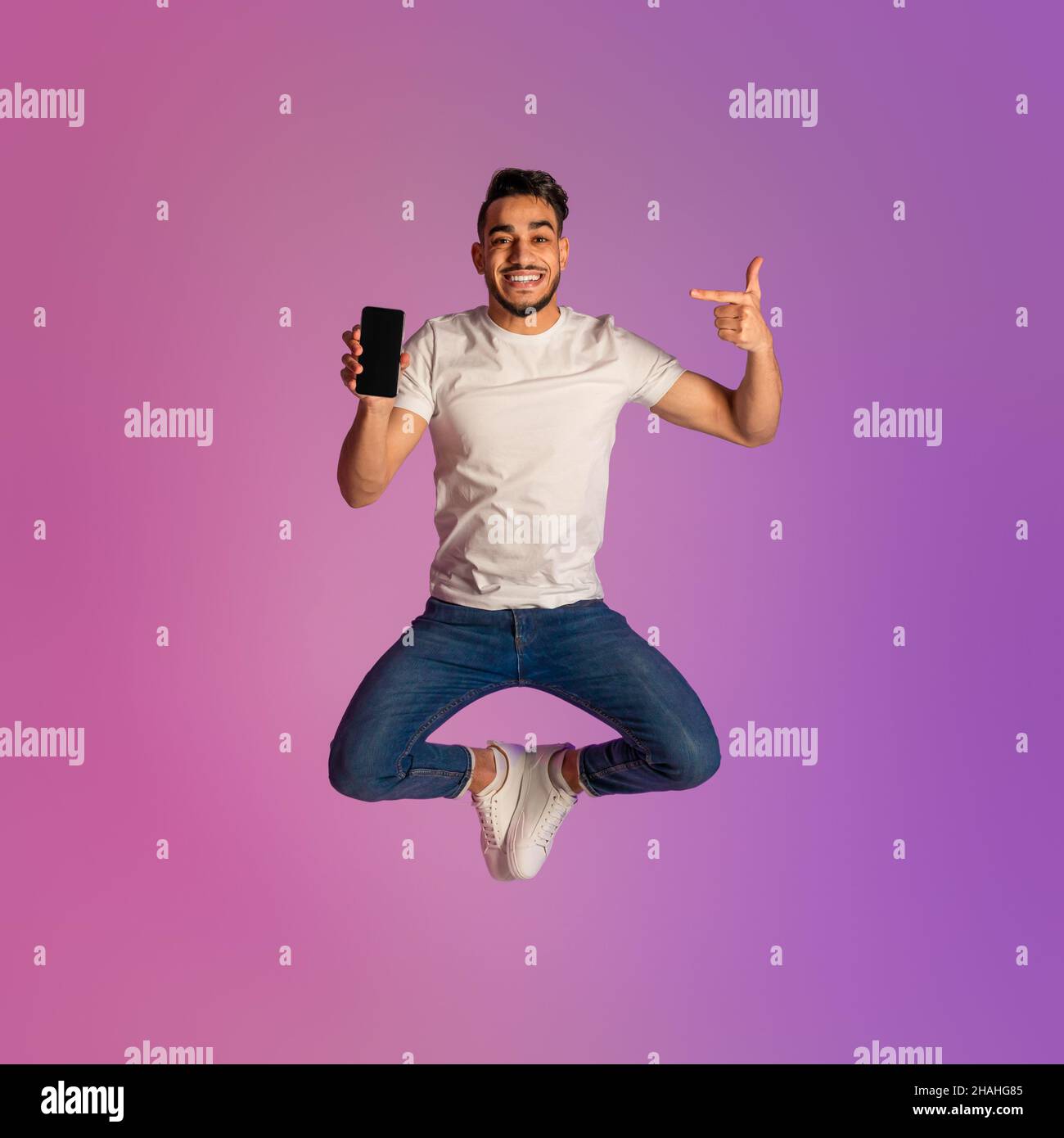 Funky young Arab guy jumping and showing modern smartphone with empty ...