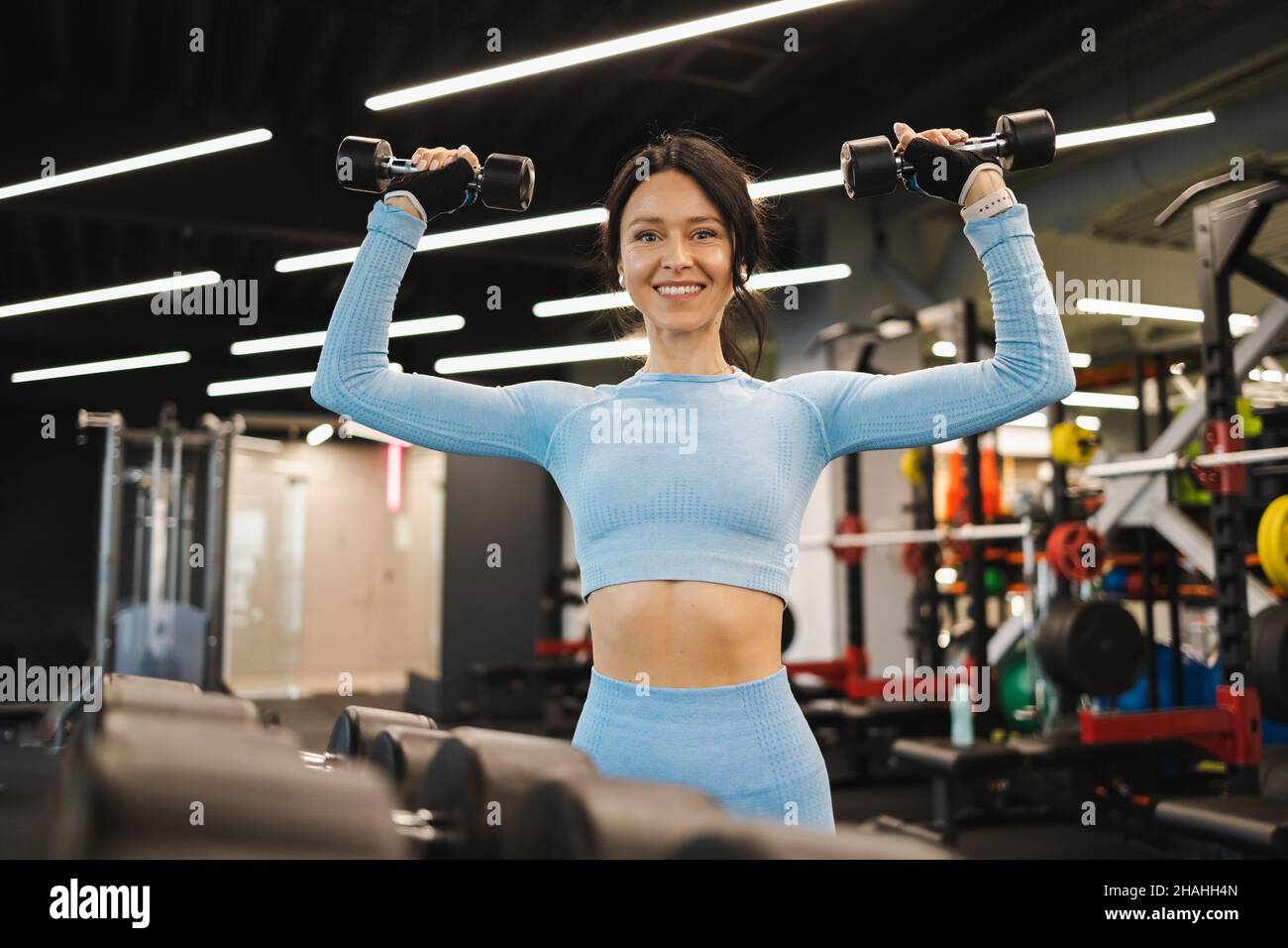 Cheerful slender woman stands in a gym with raised dumbbells up Stock ...