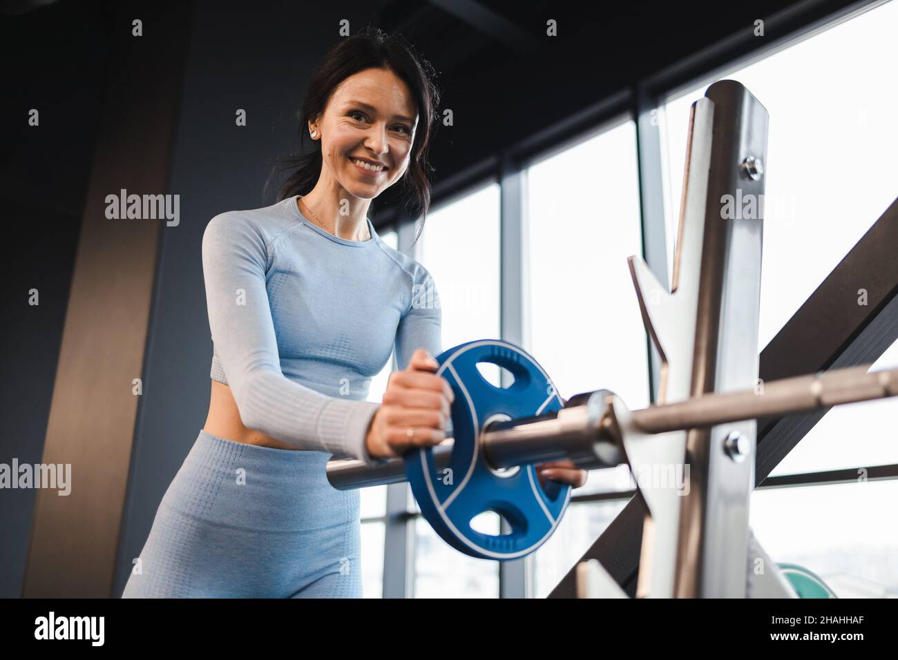 Cheerful fitness woman putting a metal disc on barbell during workout ...