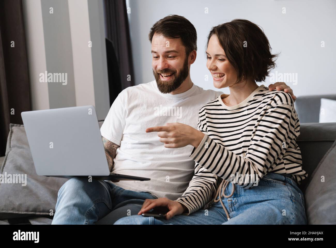 Happy young white couple looking at laptop computer sitting on a couch ...