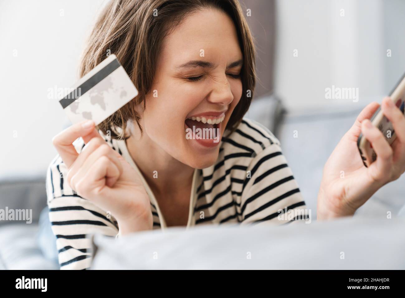Happy young white woman laying on a couch holding mobile phone at home ...