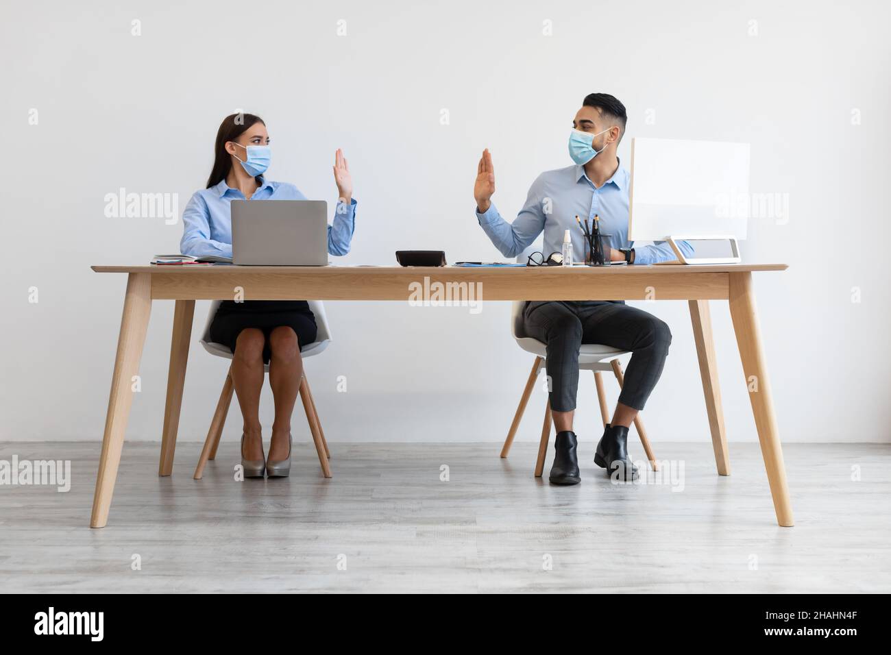 Colleagues in disposable face masks greeting each other waving hands ...