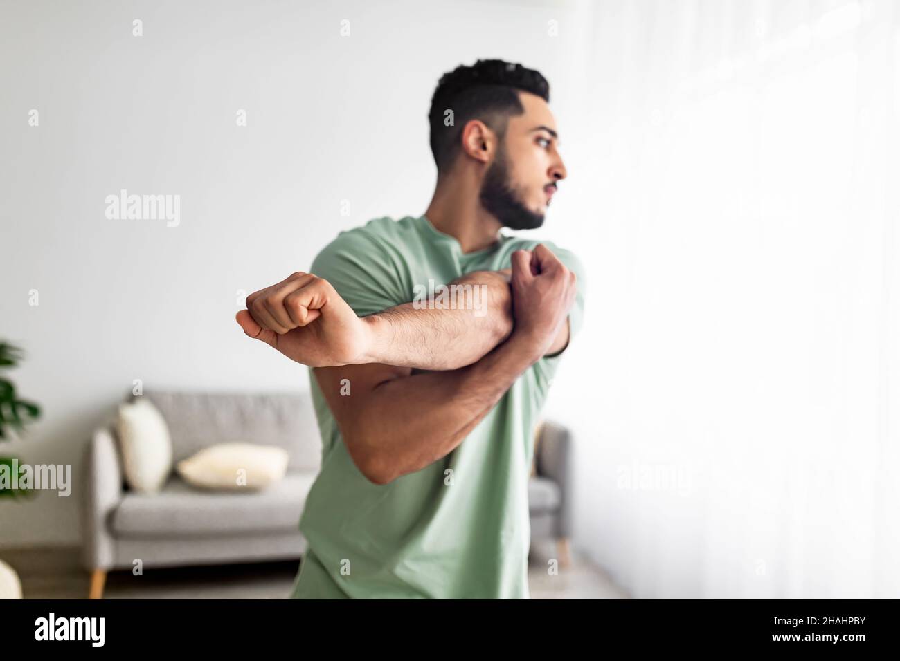 Athletic young Arab guy stretching arm muscles, doing warmup exercises ...