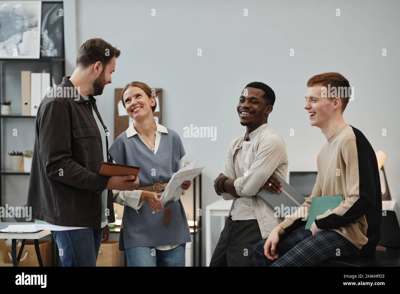 Group of young colleagues laughing and talking to each other while ...