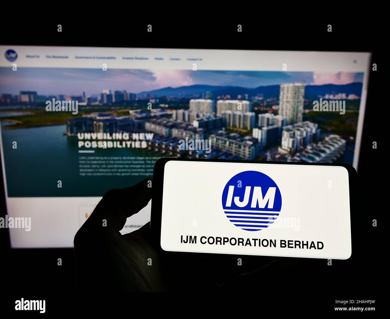 Person holding mobile phone with logo of Malaysian conglomerate IJM ...