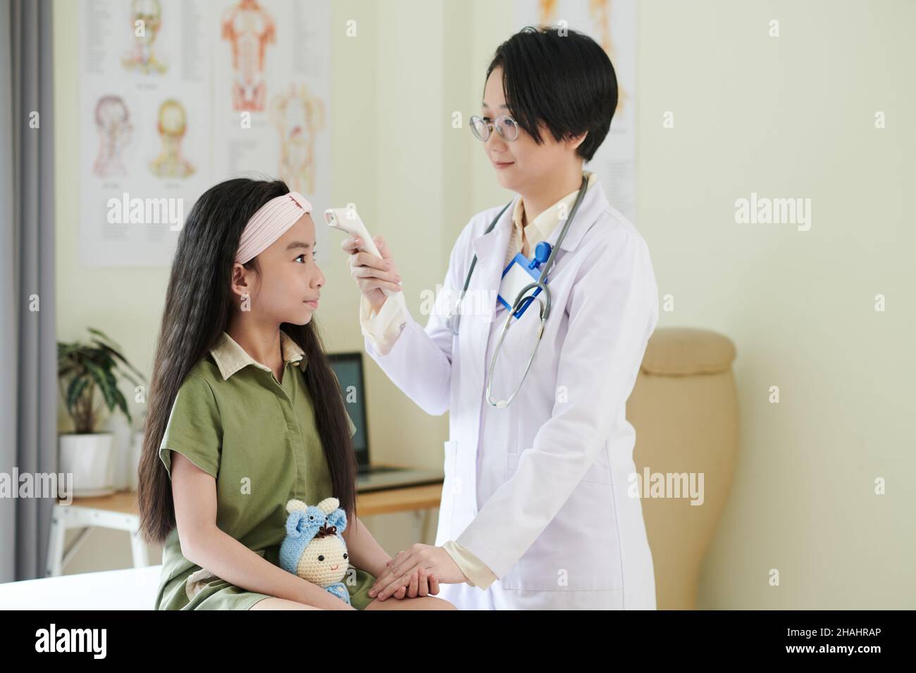 Smiling doctor holding hand of preteen girl when checking body ...