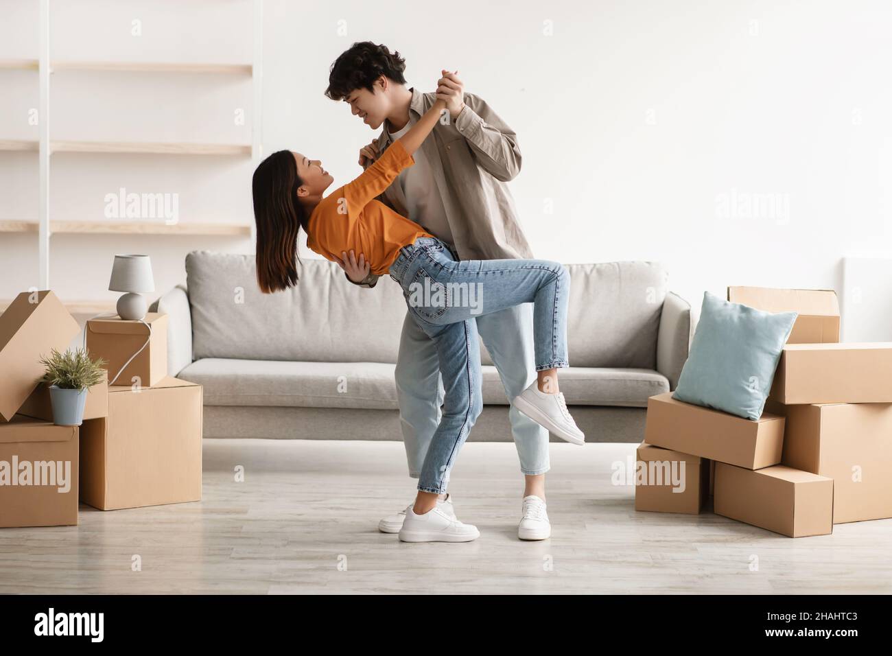 Affectionate Young Asian Couple Dancing In Their House Among Cardboard