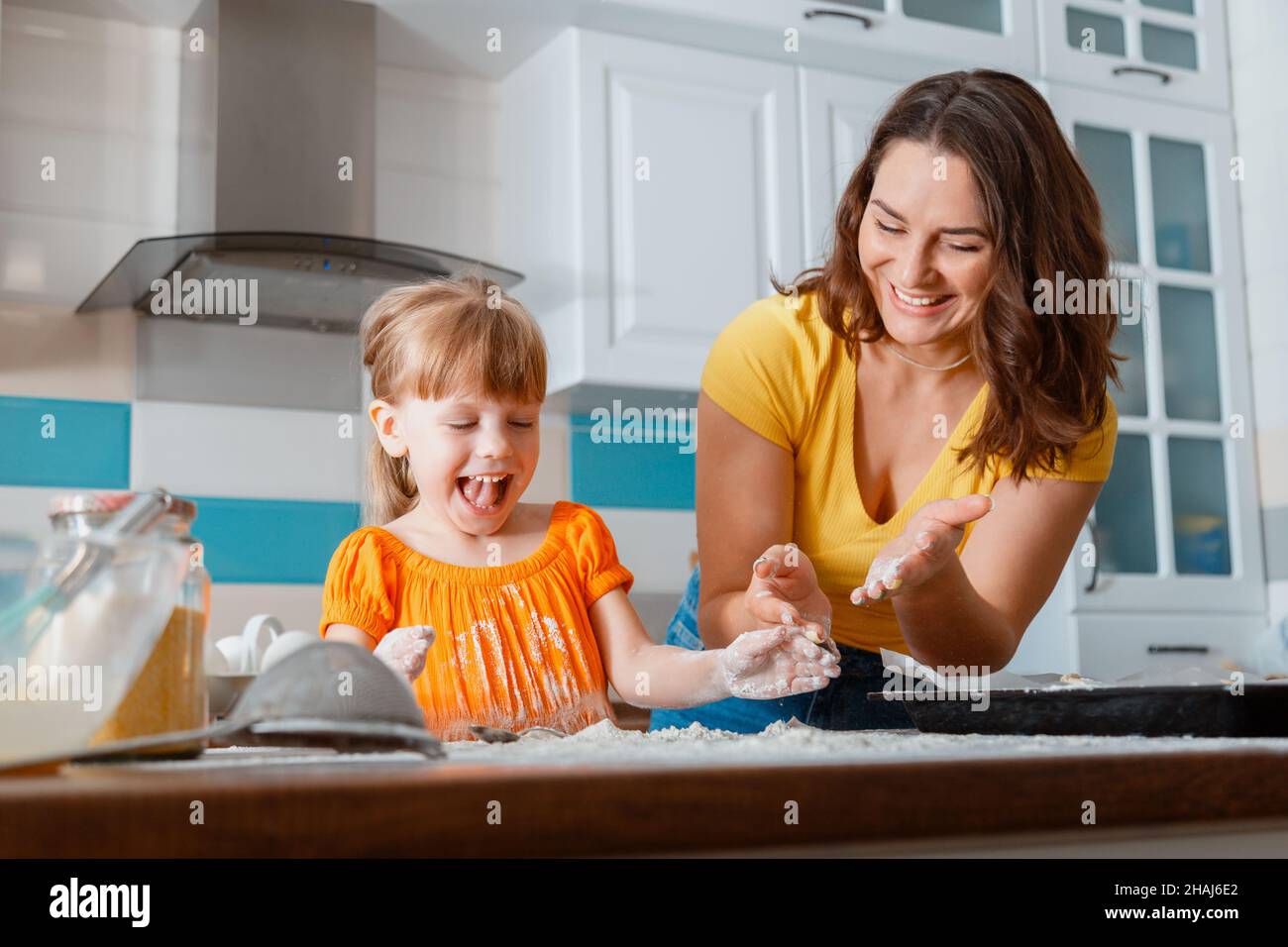 Happy laughing mother and daughter preparing baking throw flour in ...