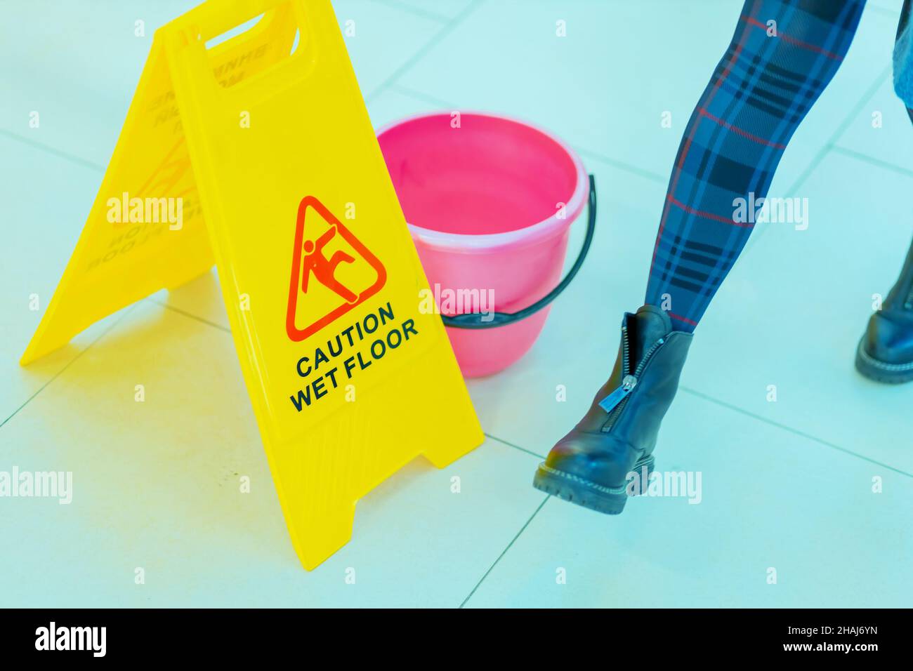 A warning sign reading caution wet floor and feet of a slipping woman ...