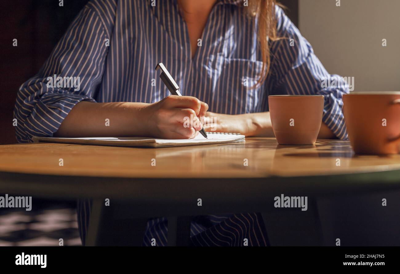 Female hand with pen taking notes, writing plans in diary on wood table ...