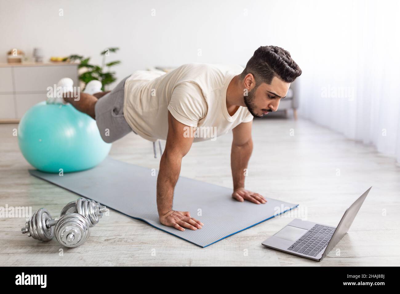 Strong Arab guy standing in plank in front of laptop, using fitness ...
