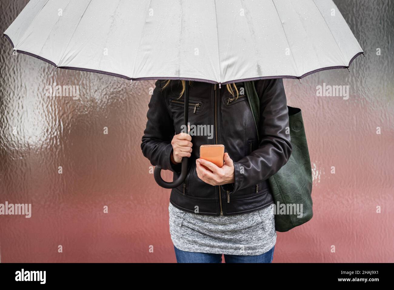 Woman with umbrella holding smart phone and standing in rain in city ...