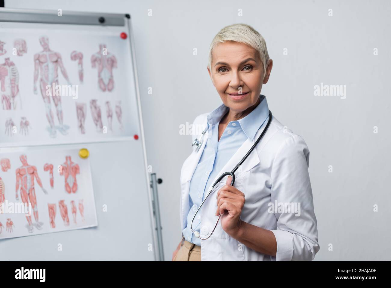 happy senior doctor in white coat with stethoscope standing near flip ...