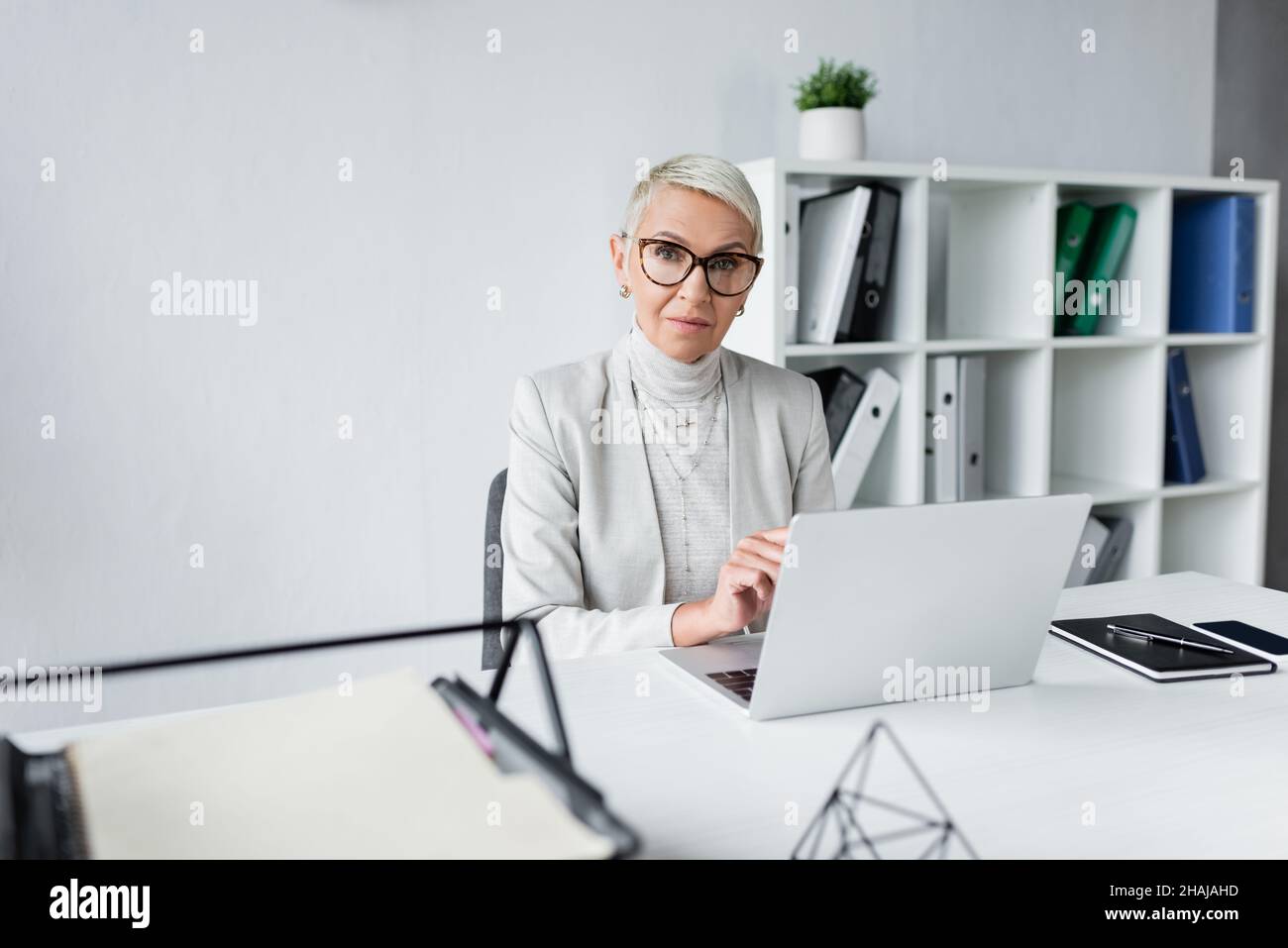 businesswoman with grey hair in glasses and suit working in office ...