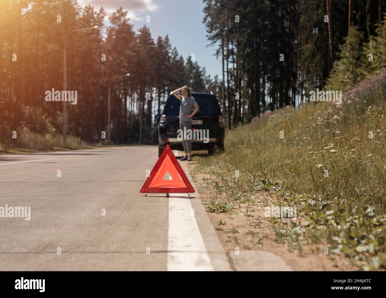 Triangle caution sign on road side after car break down and sad female ...