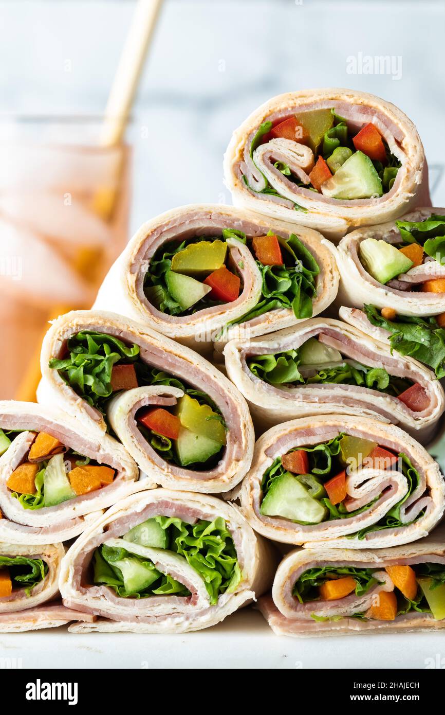 A leaning pile of fresh deli wraps with a glass of sparkling juice in ...