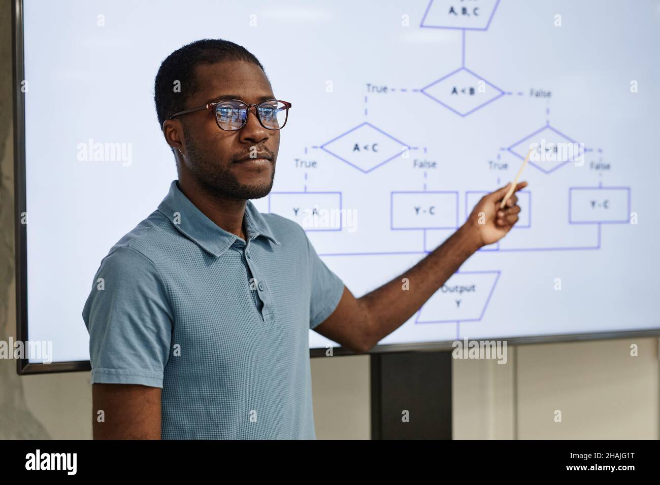 Portrait of male African-American teacher pointing at screen in coding ...