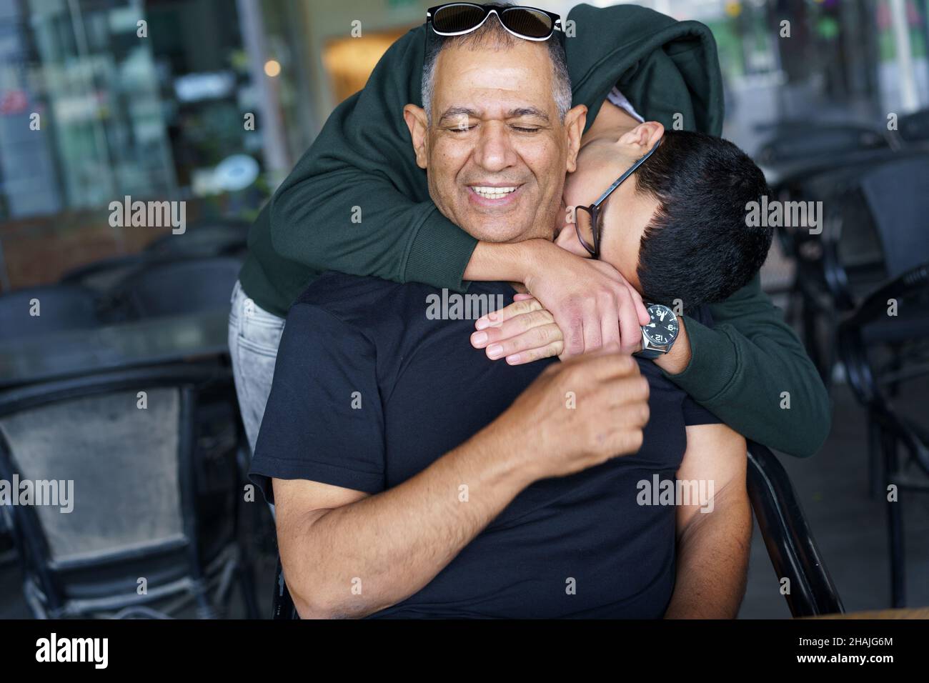 Hug for dad. A teen boy leans over to hug his father, who to be smiling ...